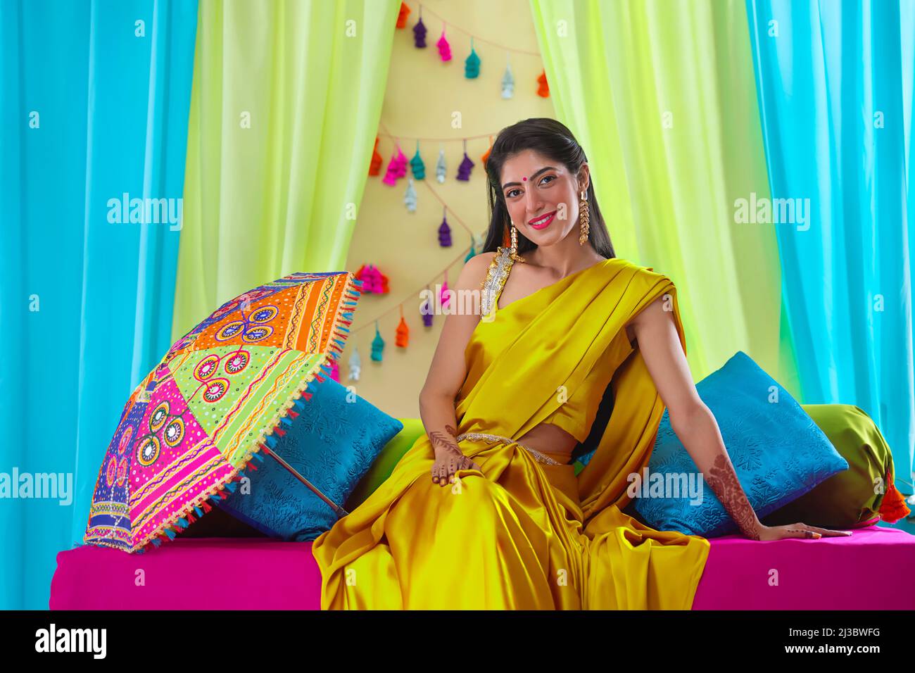 Indian bride in yellow saree sitting on stage and looking at camera ...