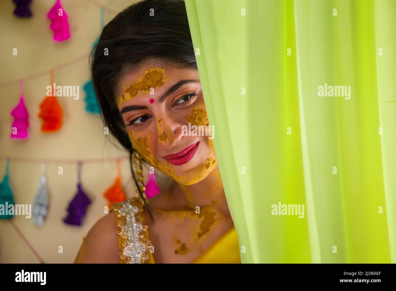 A close-up portrait of an Indian bride peeking out from behind a green ...
