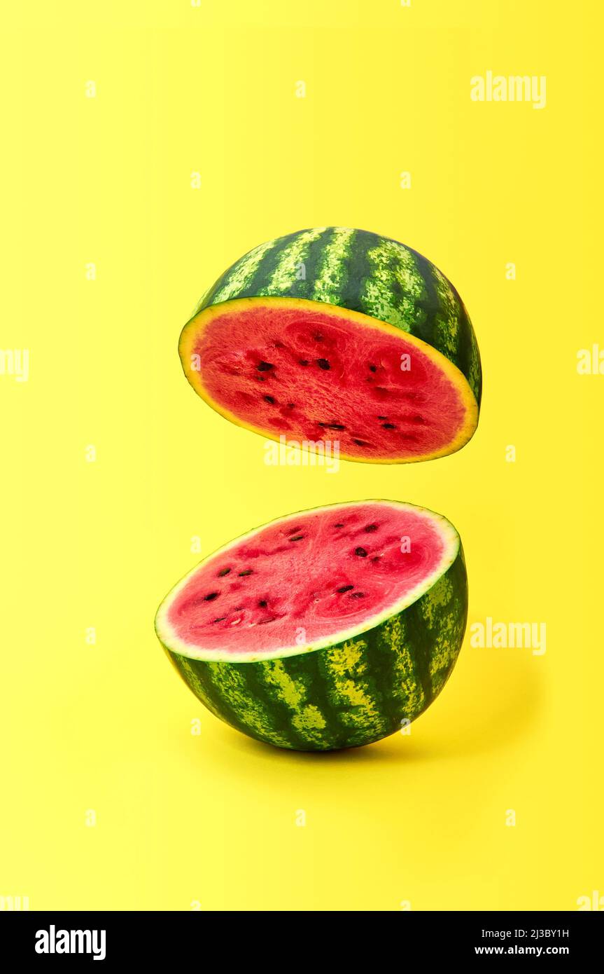 Ripe watermelon cut in half flying in the air on yellow background ...