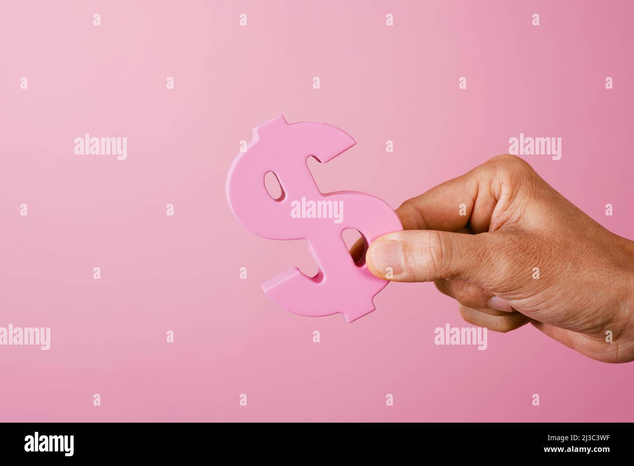 a young man grabs a pink dollar sign in front of a pink background ...