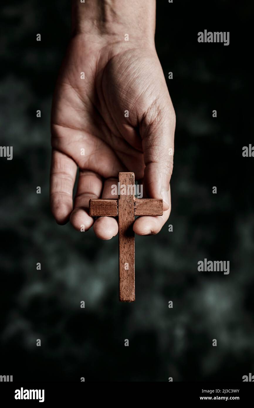 closeup of a man with a wooden cross in his hand, on a black mottled ...