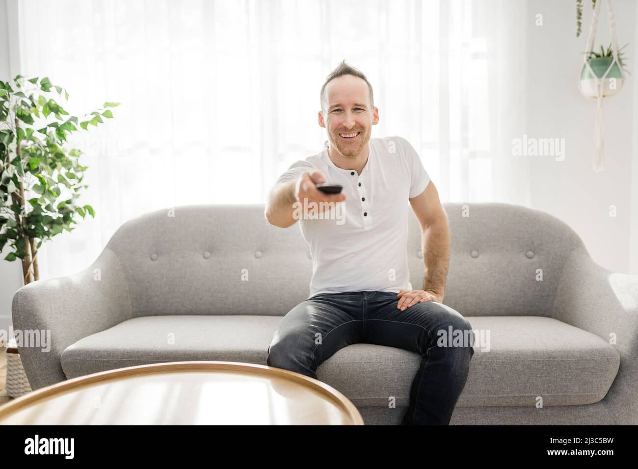 Man with remote control on the sofa at home Stock Photo - Alamy
