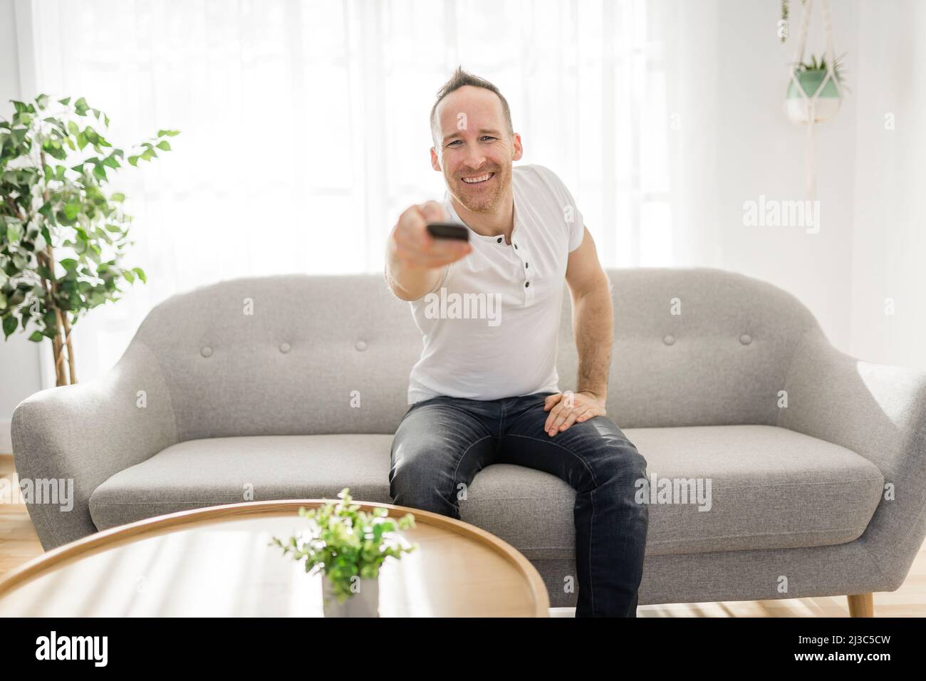 Man with remote control on the sofa at home Stock Photo - Alamy