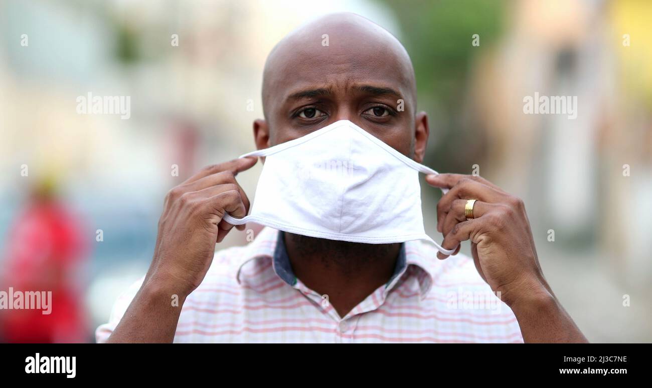 African man putting covid-19 face mask outside in urban street Stock ...