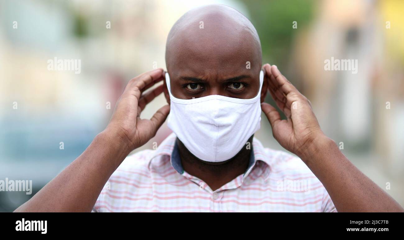 African man putting covid-19 face mask outside in urban street Stock ...