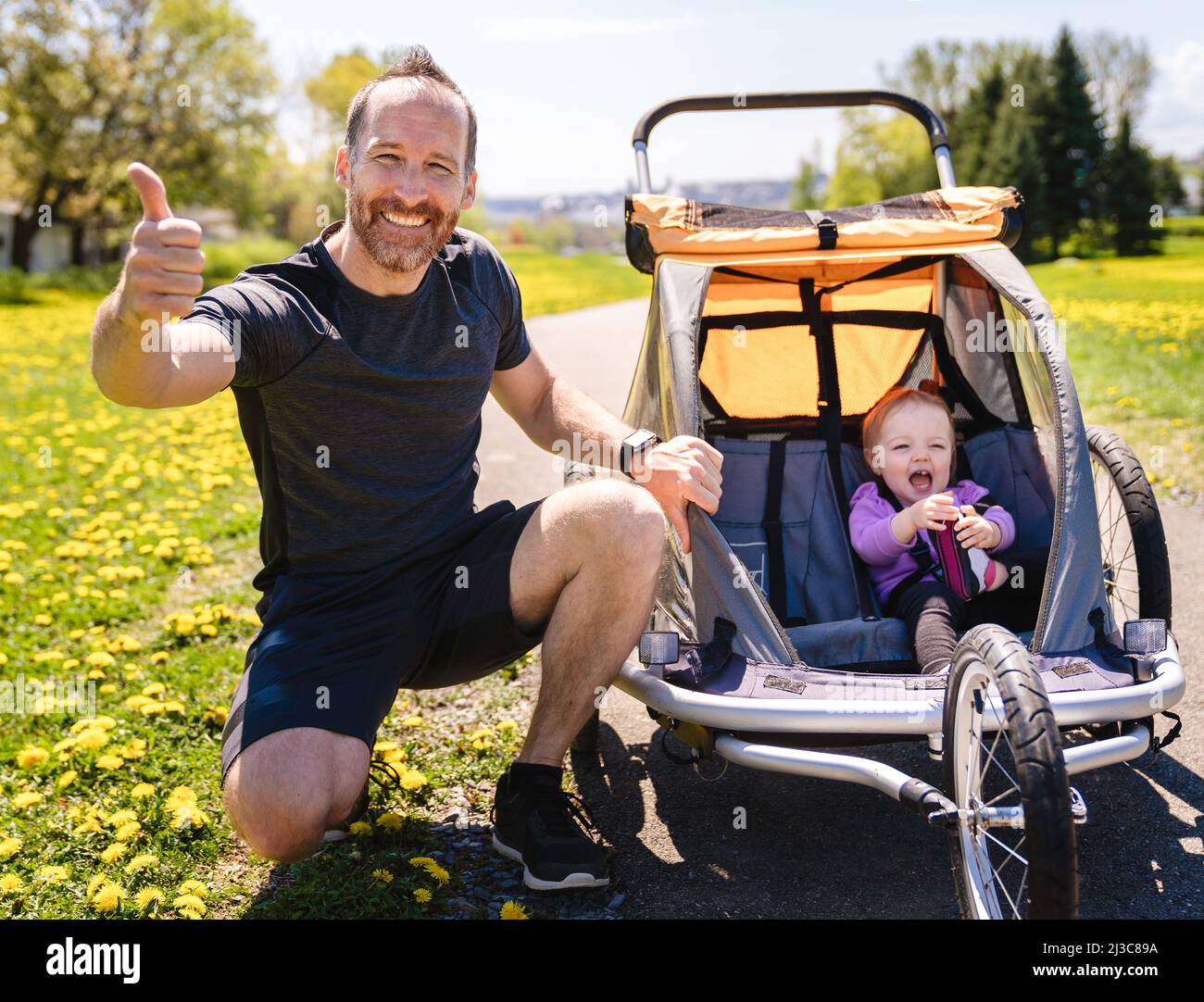 man with baby in jogging stroller running outside in summer season ...