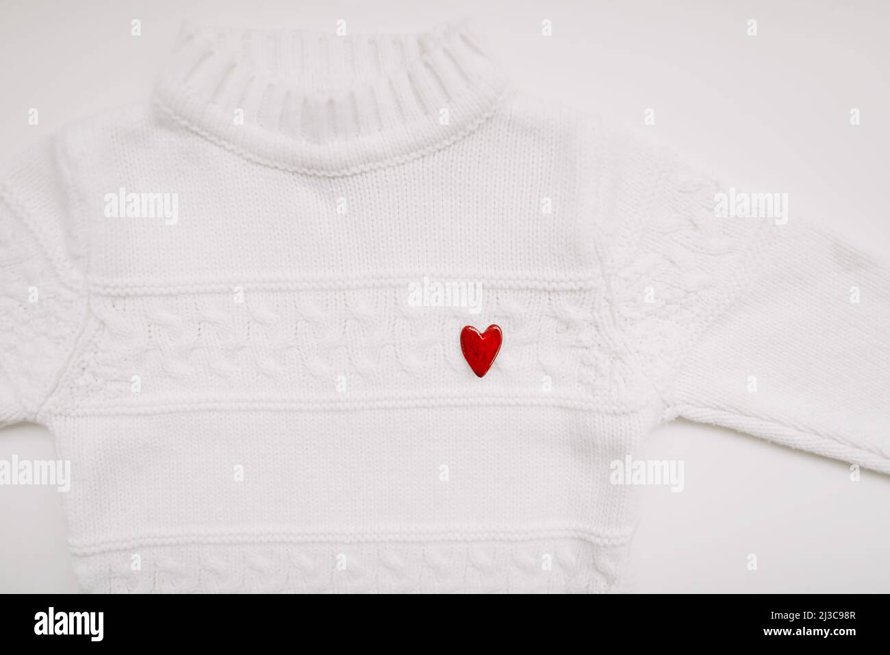 White woolen sweater with a red heart shaped pin on white background ...