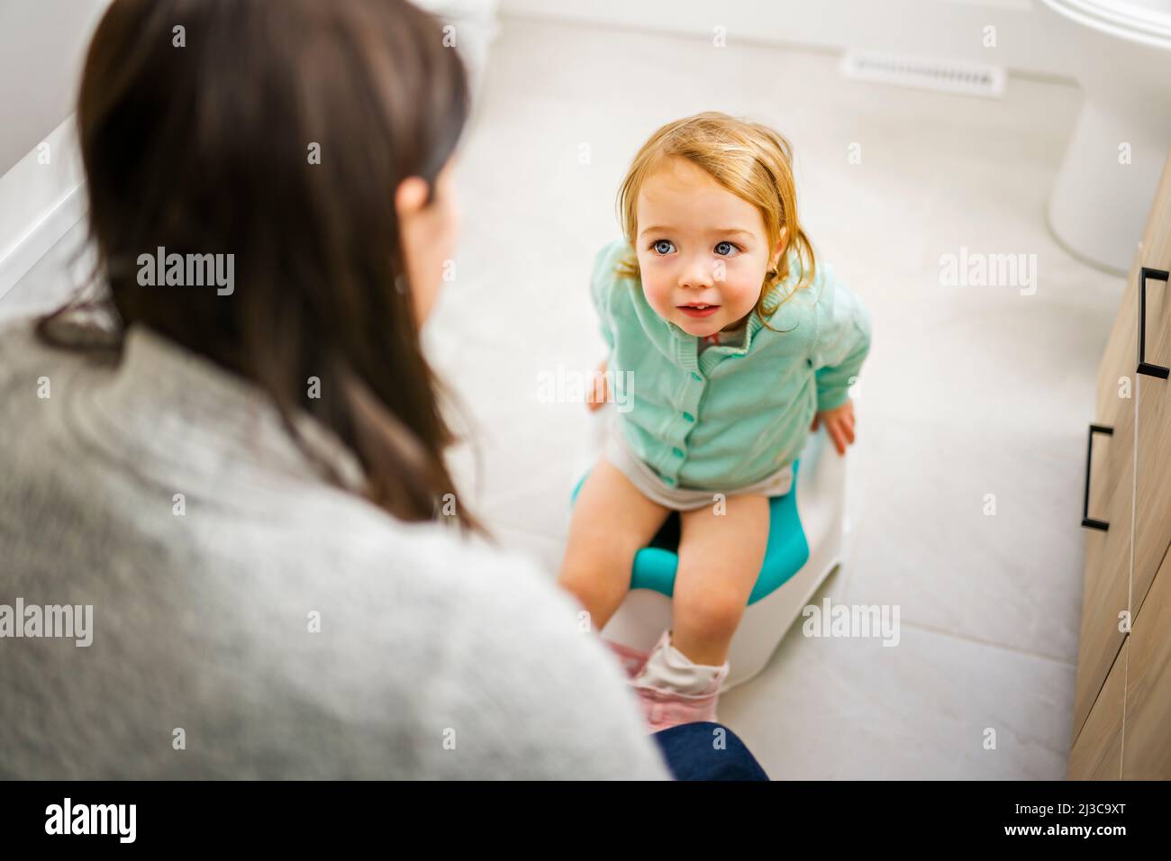 cute child girl sitting on chamberpot on the bathroom look at is mother ...