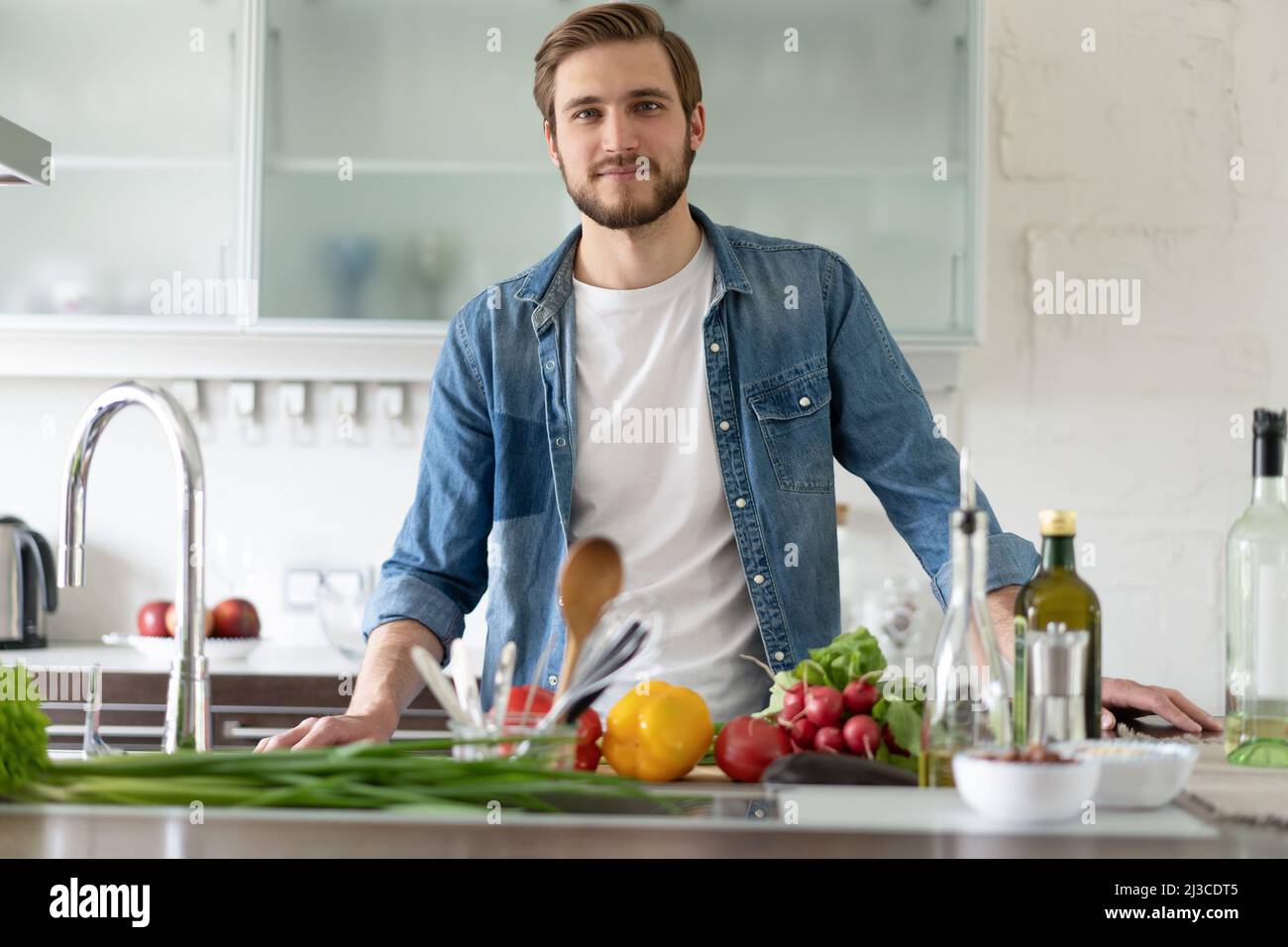 Handsome smiling young man leaning on kitchen counter with vegetables ...