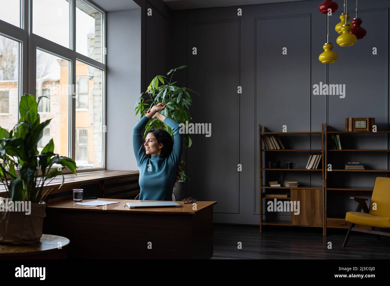 Happy female employee doing stretching exercises at workplace, feeling ...