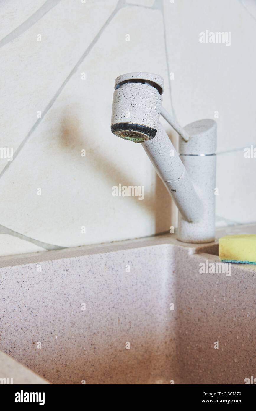 Ceramic beige kitchen faucet over a stone sink. An old dish sponge next ...
