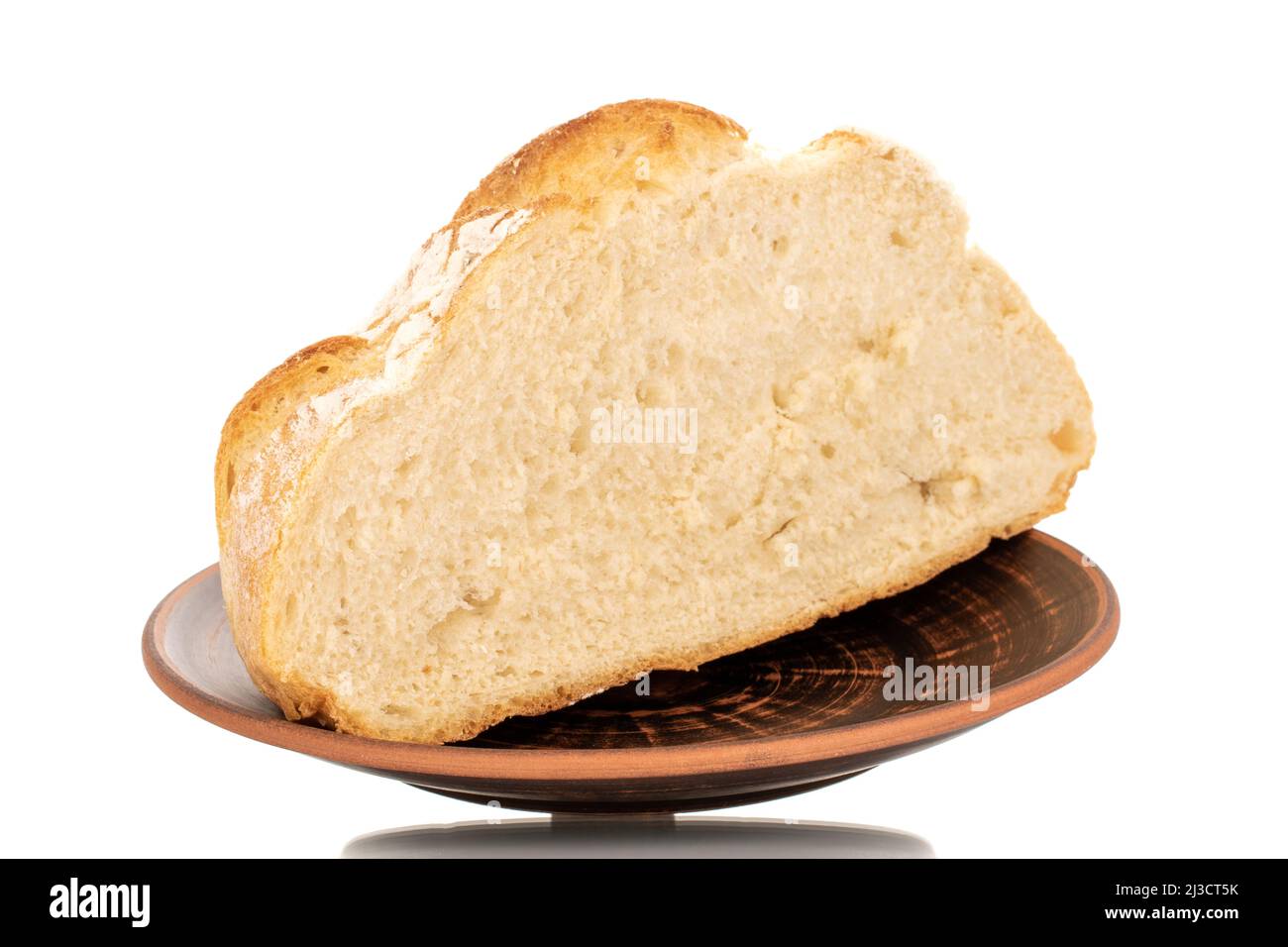 One half of a loaf of fresh fragrant white wheat bread on a clay plate ...
