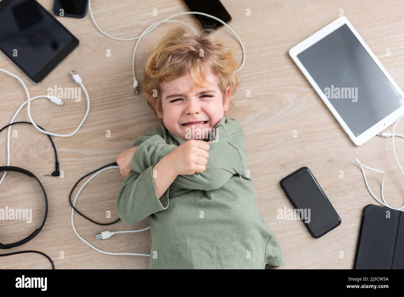 Top view of unhappy boy crying while lying on floor near abundance of ...