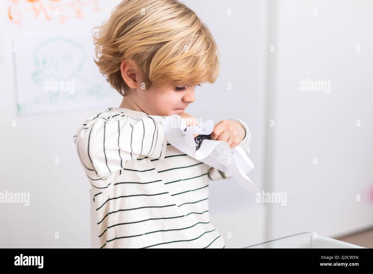 Unhappy boy tearing up drawing with black strokes while sitting at ...