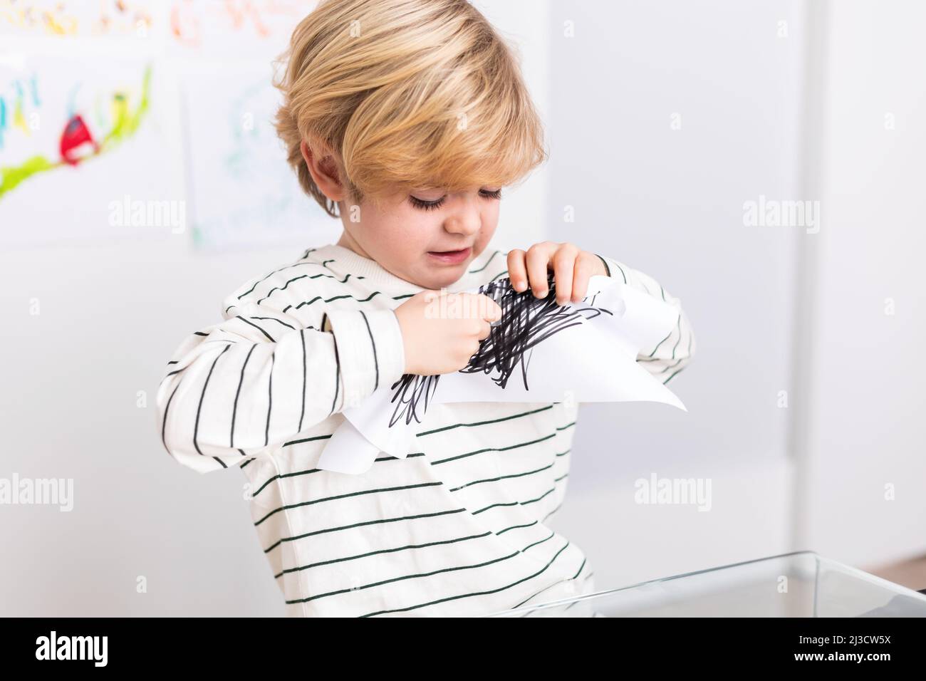 Unhappy boy tearing up drawing with black strokes while sitting at ...