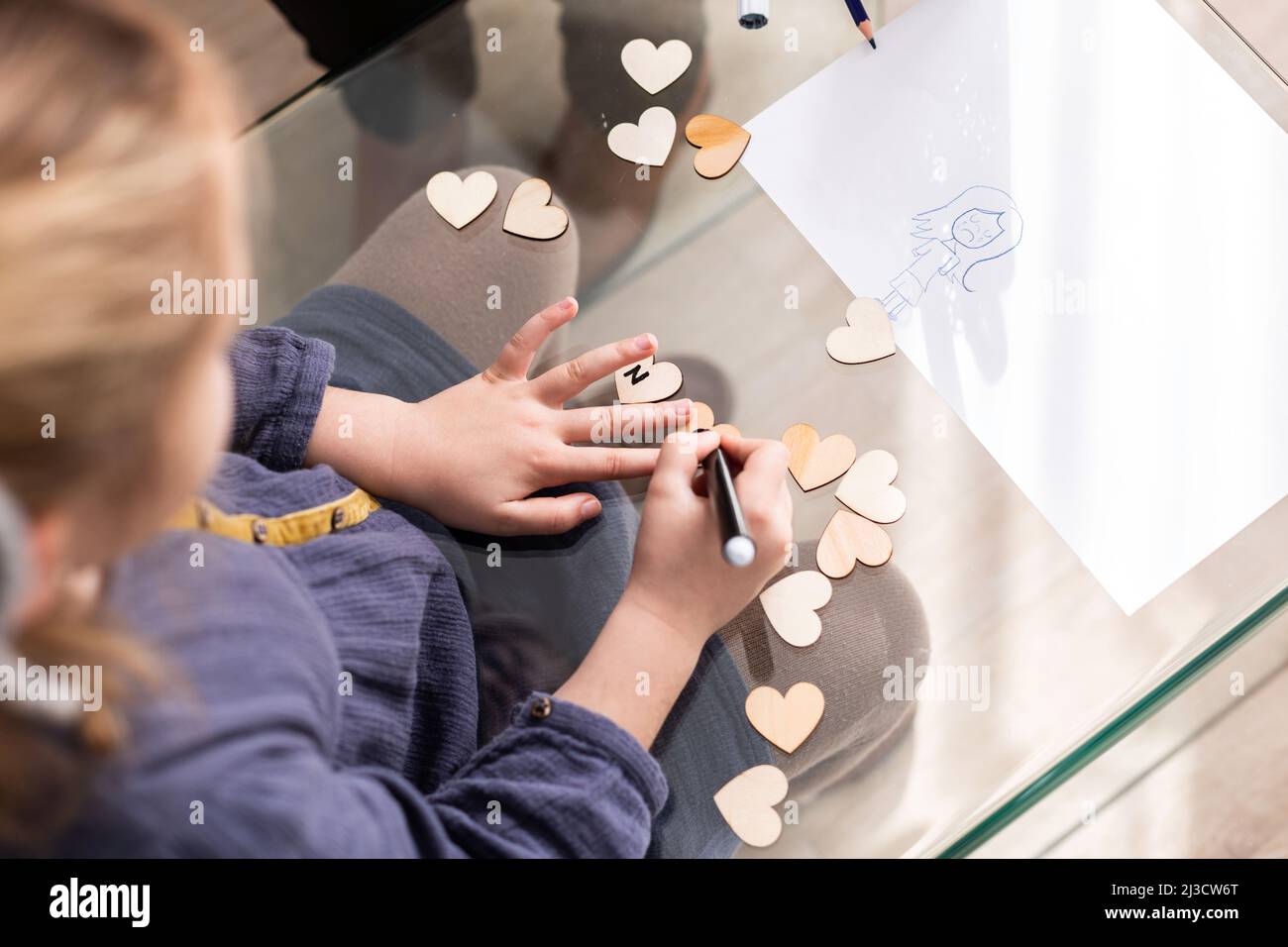 Top view of crop anonymous kid writing inscription on small hearts ...