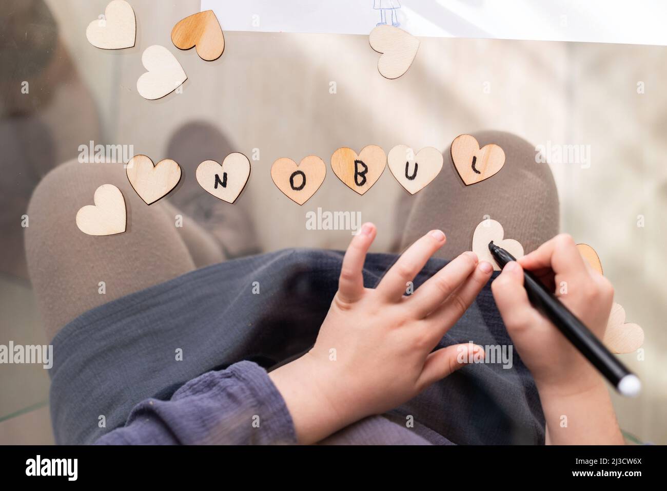 Top view of crop anonymous kid writing inscription on small hearts ...