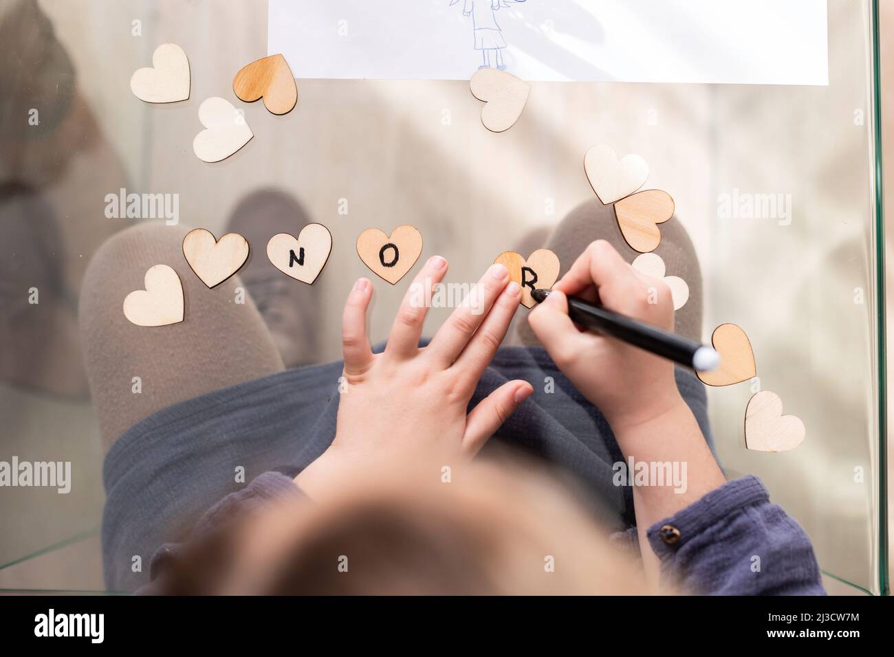 Top view of crop anonymous kid writing inscription on small hearts ...