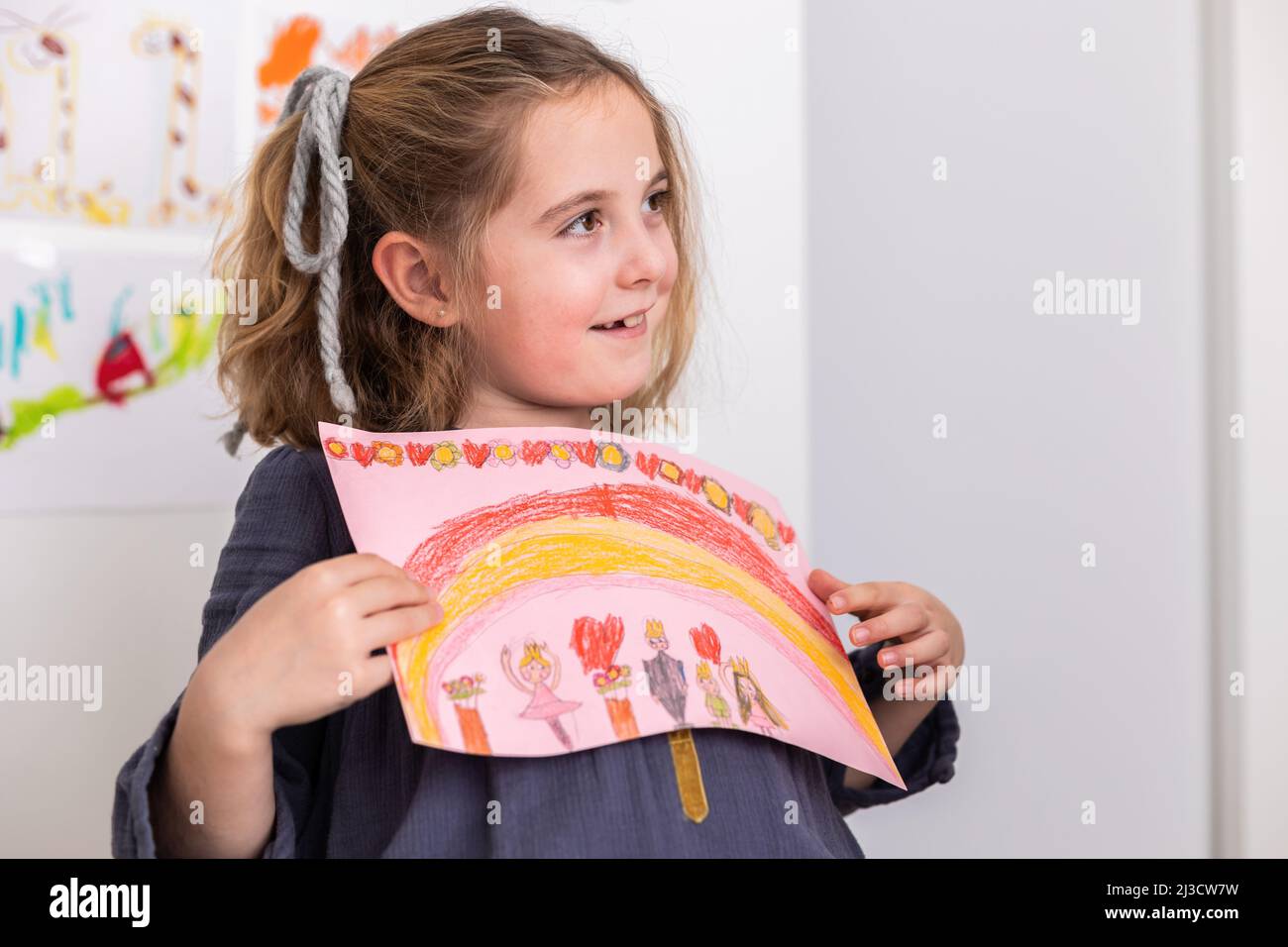 Cute smiling girl pointing at colorful drawing sitting at table in ...