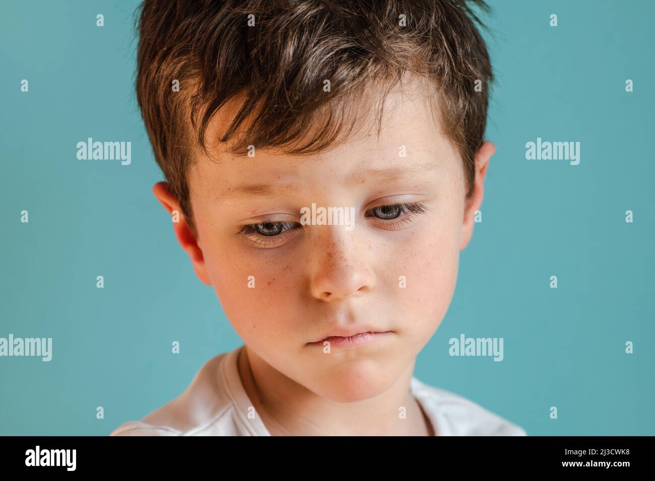 Headshot of upset boy with brown hair looking down with upset face ...