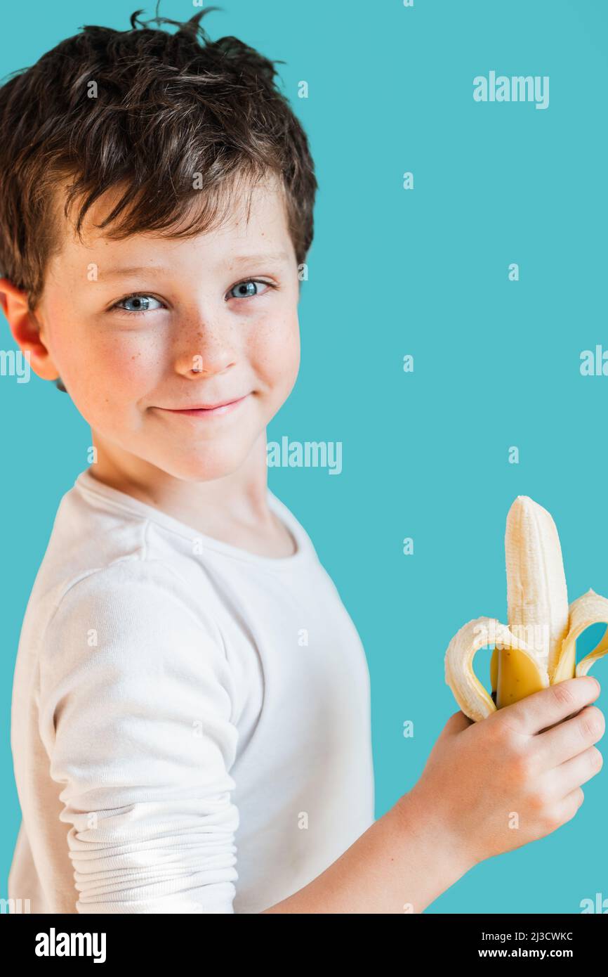 Happy boy with ripe yellow peeled tasty banana looking away with smile ...