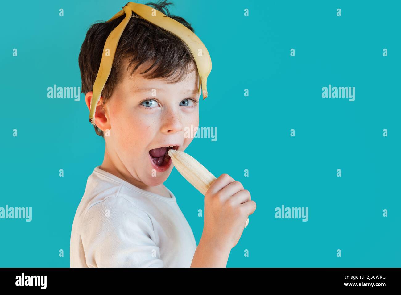 Side view of headshot of cheerful boy with banana peel on head and ...
