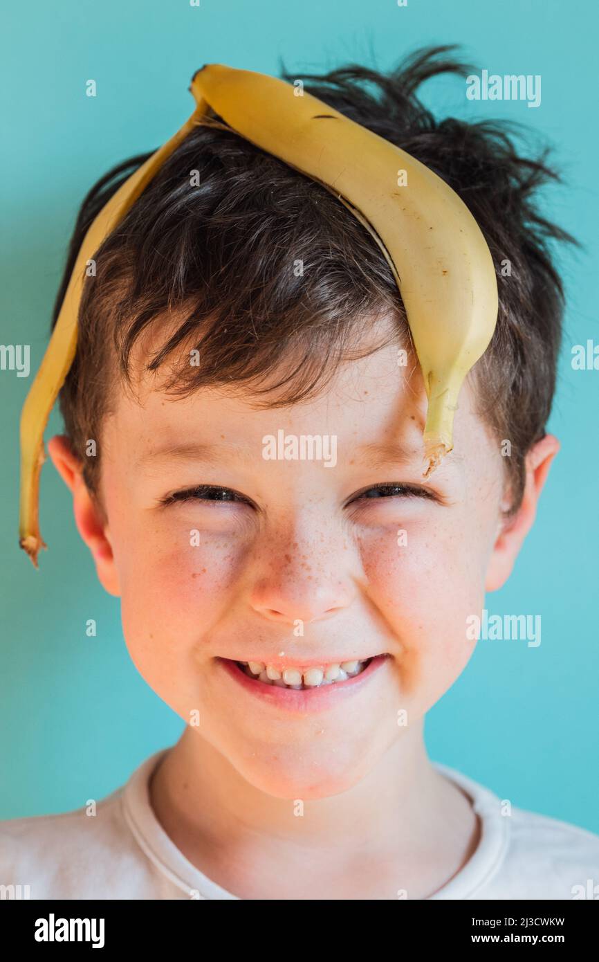 Headshot of cheerful boy with banana peel on head looking at camera ...