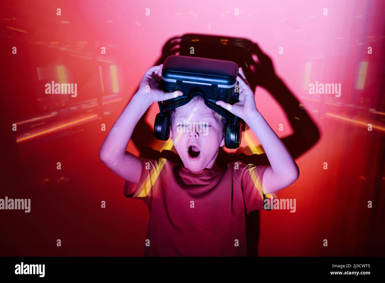 Shocked little gamer in t shirt taking off VR headset and looking down ...