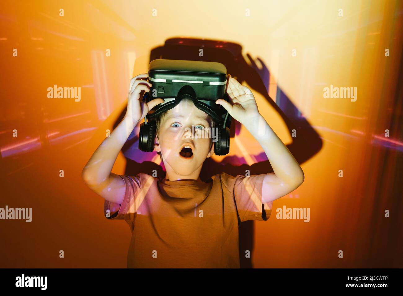 Shocked little gamer in t shirt taking off VR headset and looking at ...