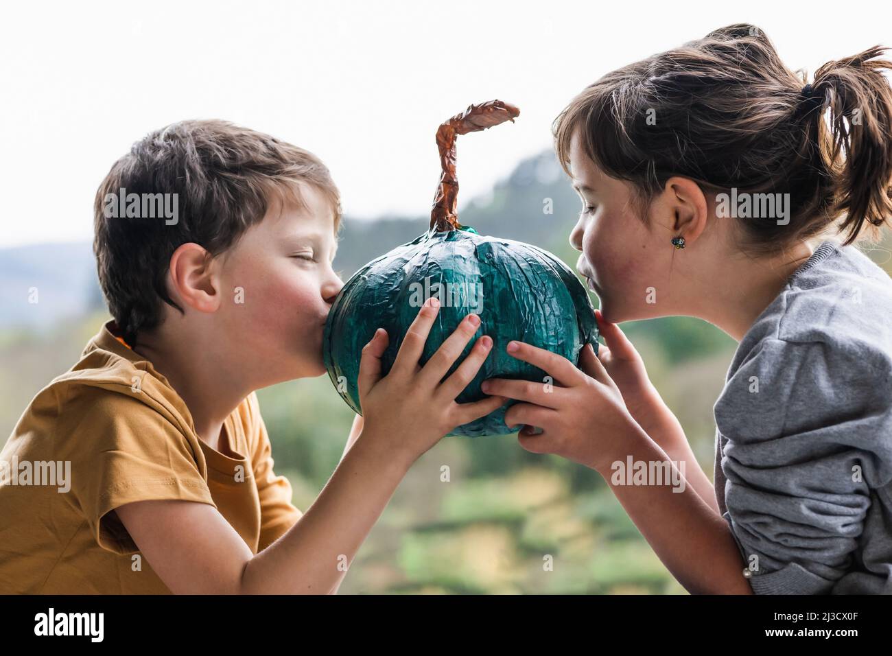 Side view of cute children kissing teal pumpkin in hands while standing ...