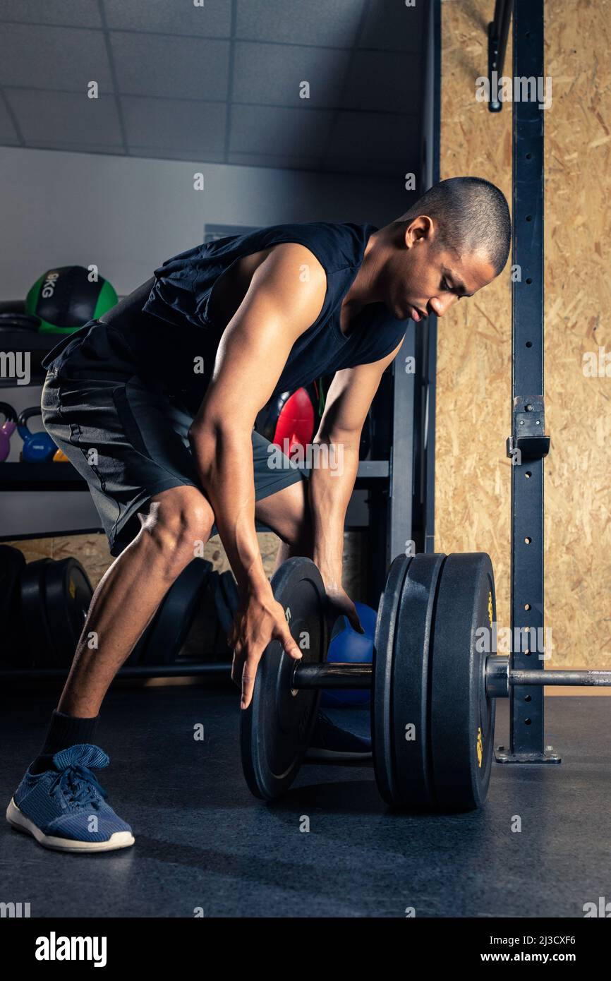 Full body side view of strong African American bodybuilder adding plate ...