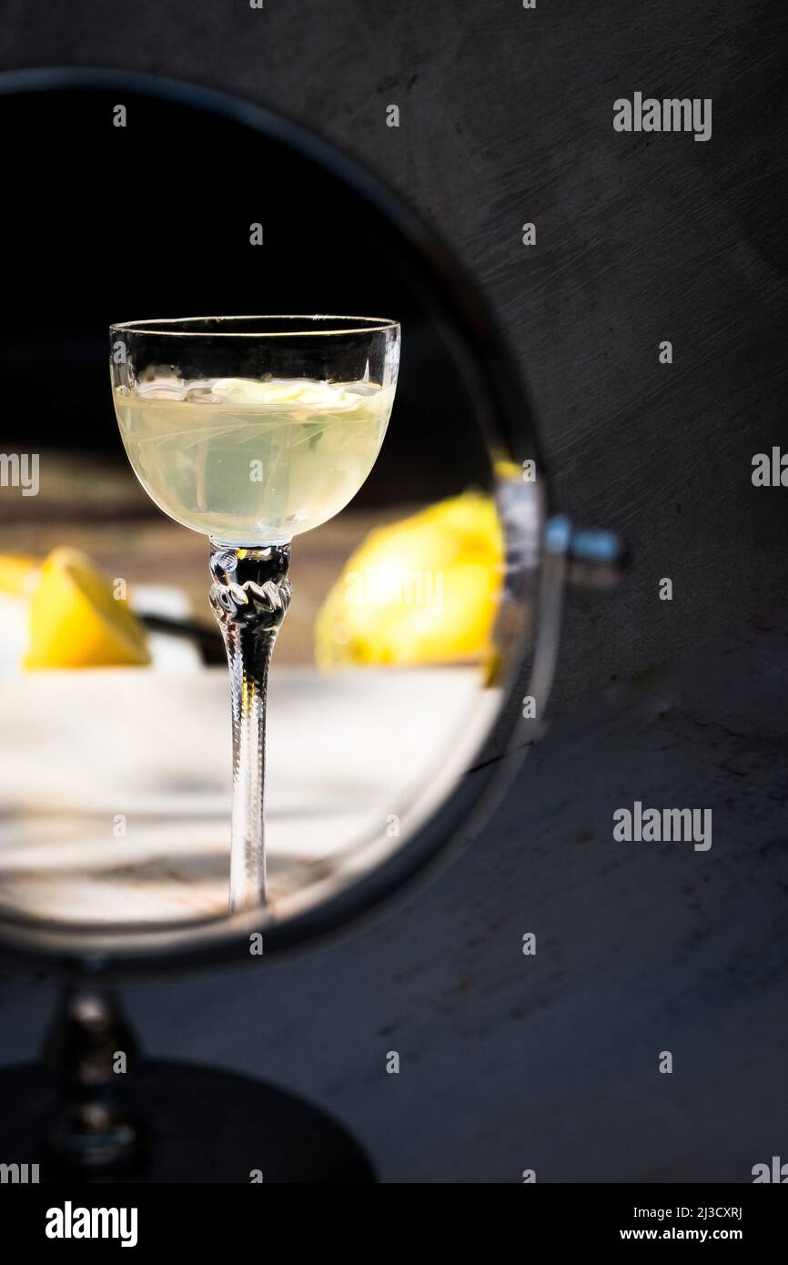 Glass goblet of cold lemon cocktail reflecting in round mirror in dim ...