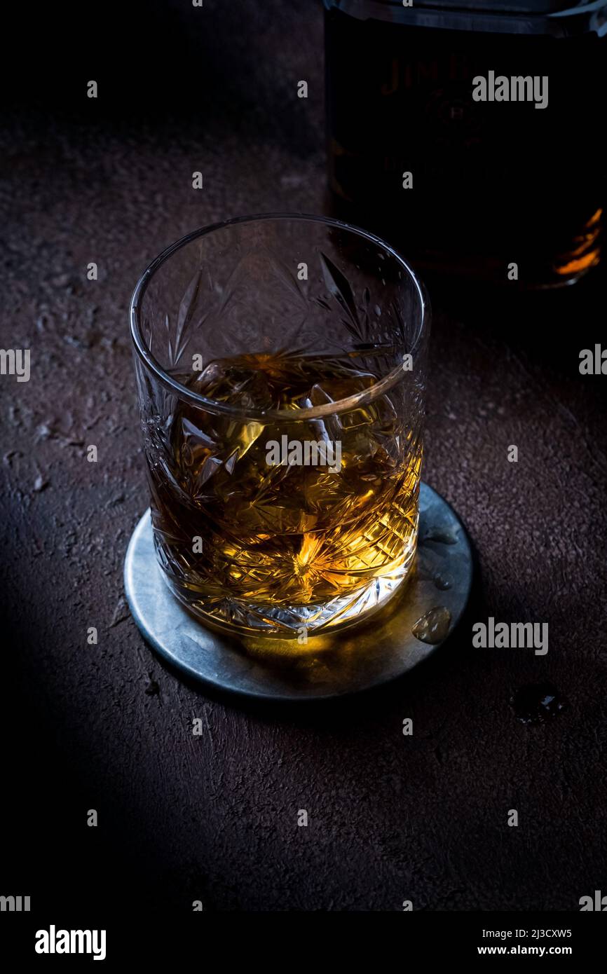 From above glass cup with cold whiskey and cubes of ice placed on table ...
