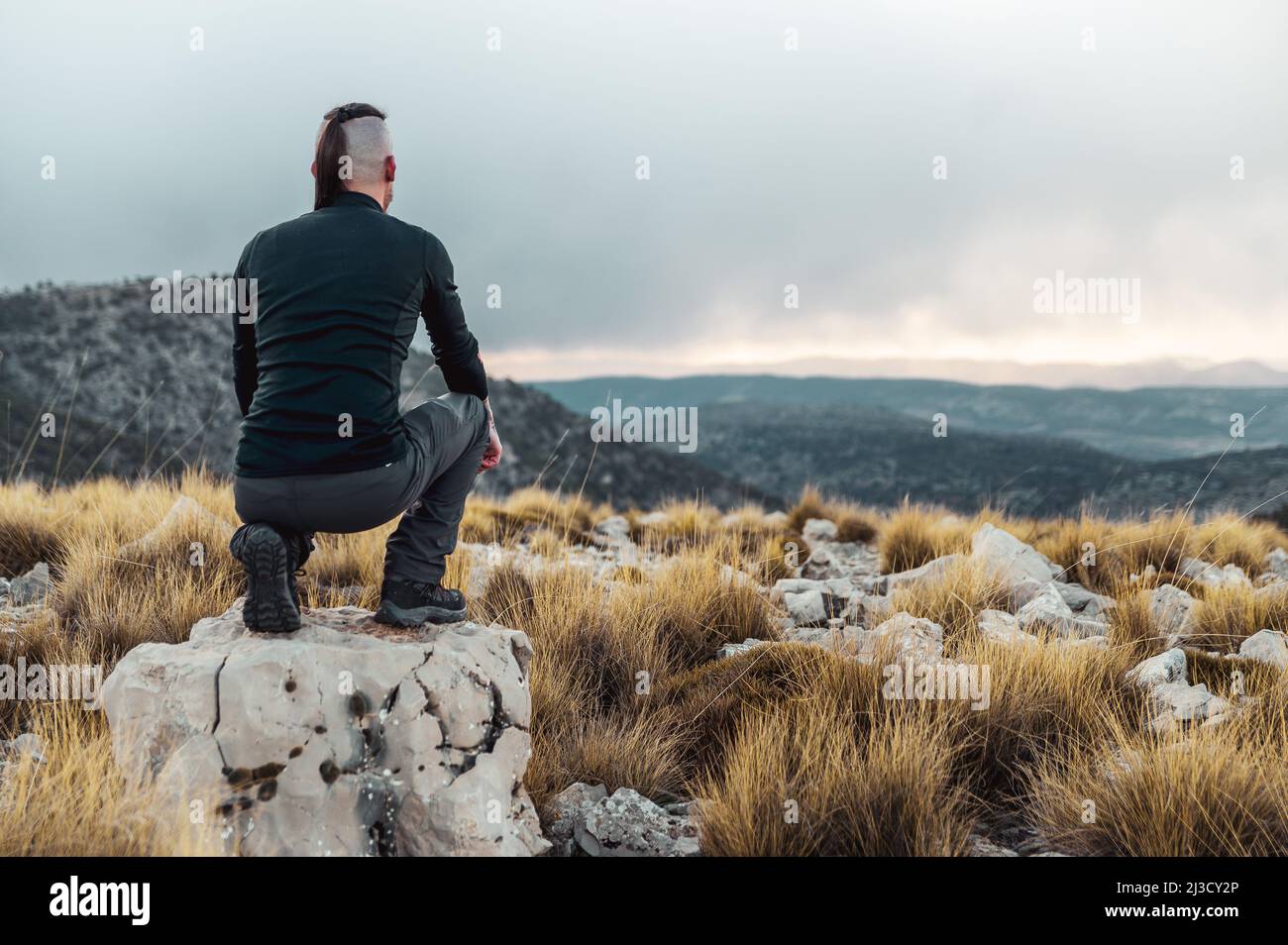 Back view full body of unrecognizable male crouching on stones in hilly ...