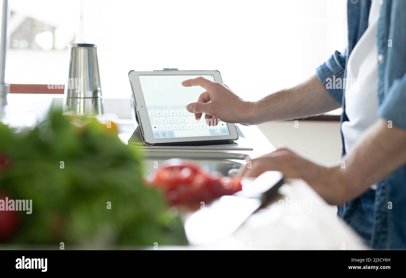 cooking, technology and home concept - man reading recipe from tablet ...
