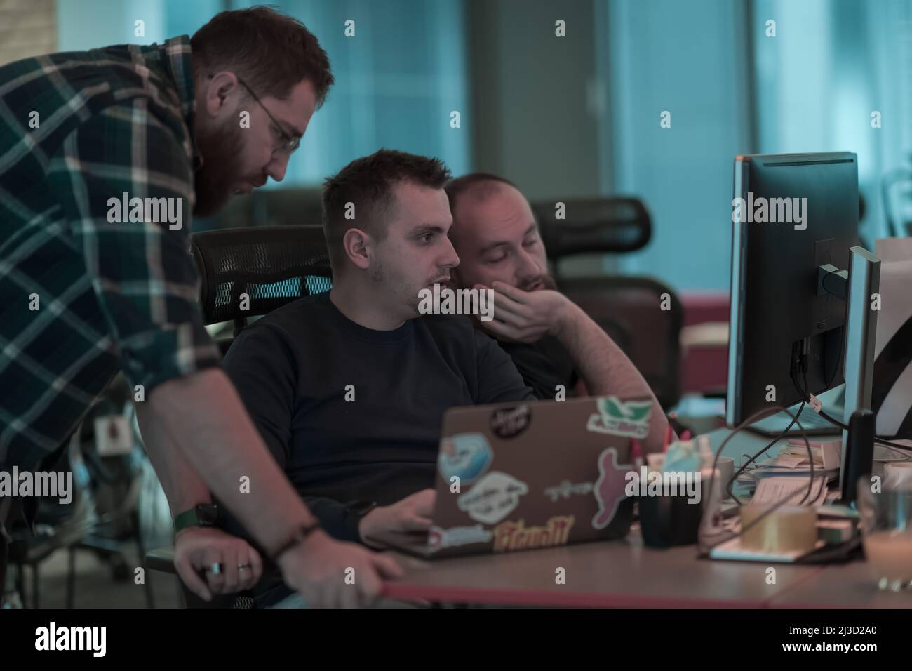 A photo of three men staring intently at a computer while sitting in a ...