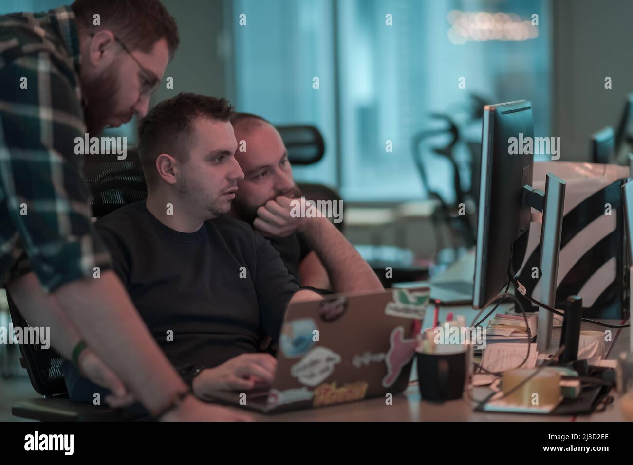 A photo of three men staring intently at a computer while sitting in a ...