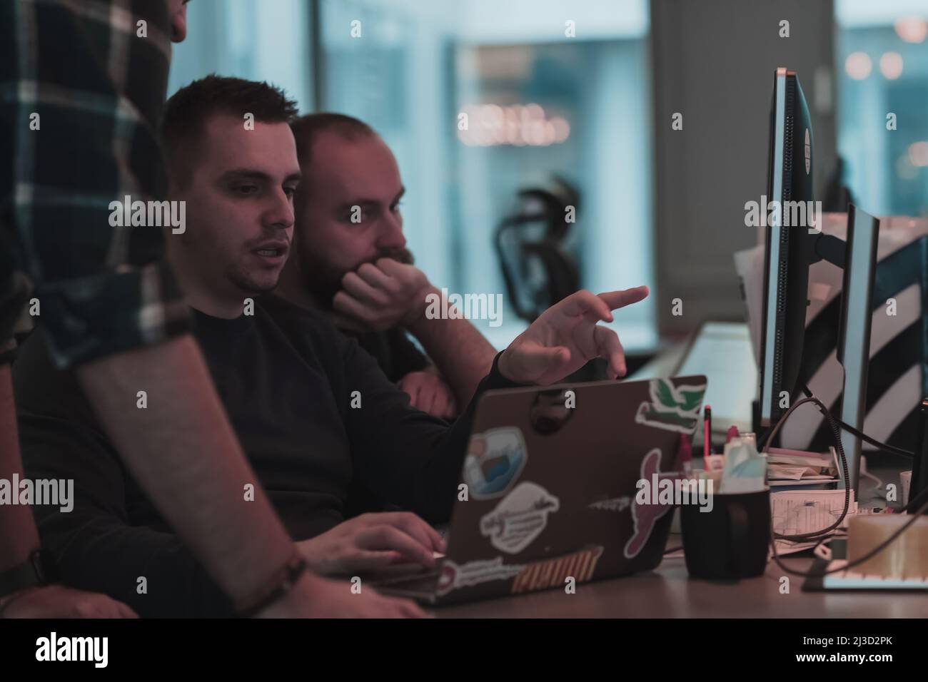 A photo of three men staring intently at a computer while sitting in a ...