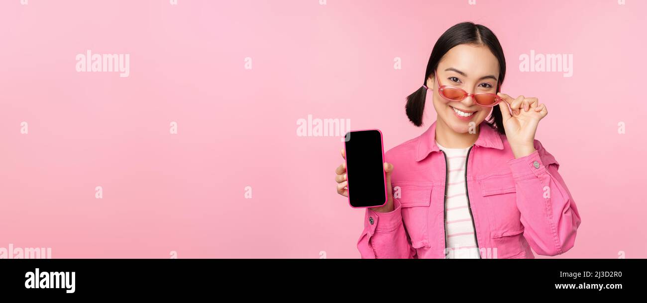 Portrait of stylish modern asian girl shows mobile phone screen ...