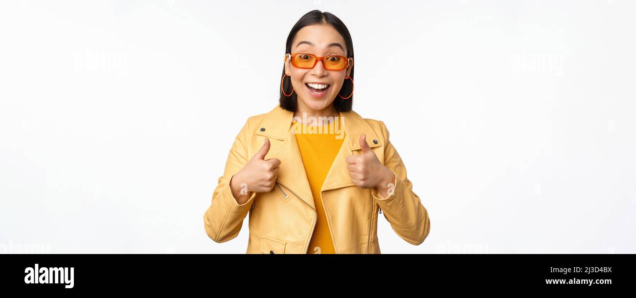 Enthusiastic asian girl smiles, shows thumbs up and looks happy, saying ...