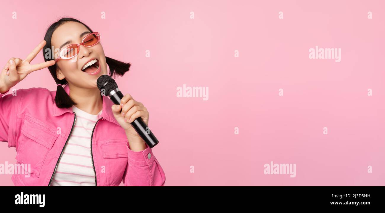 Happy beautiful asian girl singing with mic, using microphone, enjoying ...