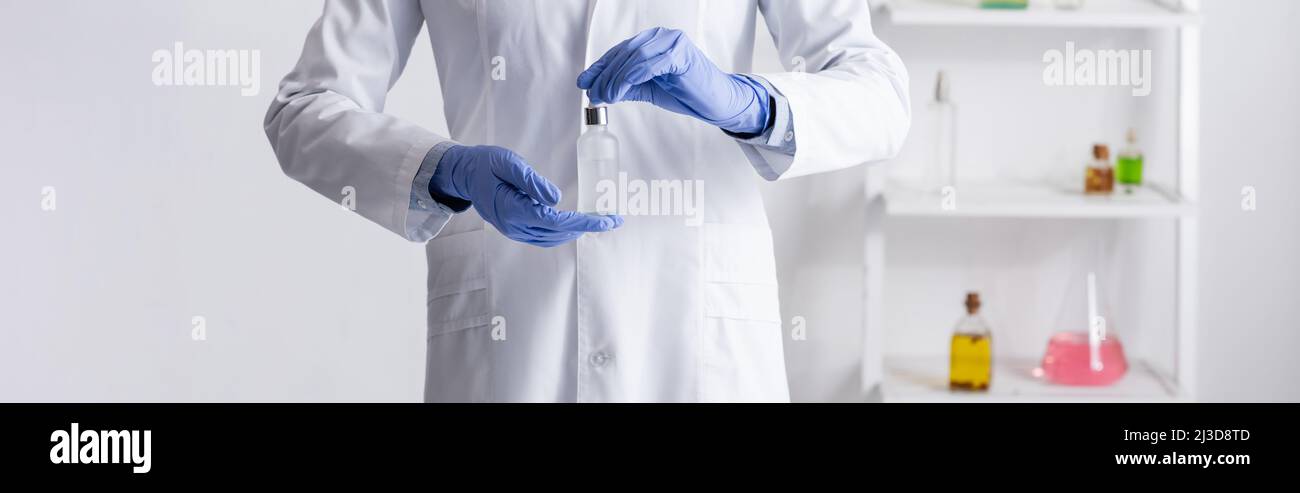 cropped view of laboratory assistant in latex gloves holding bottle ...