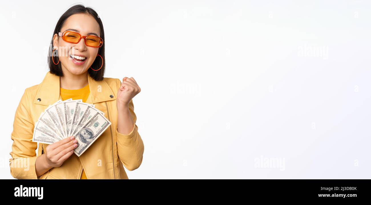 Stylish smiling asian girl holding money cash, showing dollars and ...