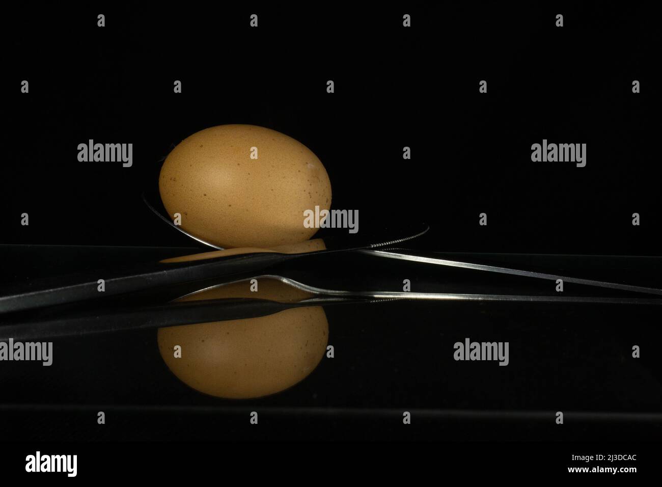 a silver table spoon and knife with a balanced egg reflected and ...