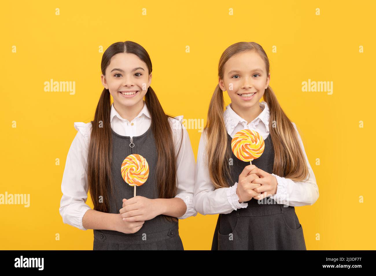 Happy kids in school uniforms hold lollipops yellow background, sweet ...