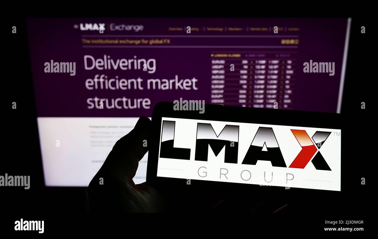 Person holding smartphone with logo of British fintech company LMAX Group on screen in front of ...