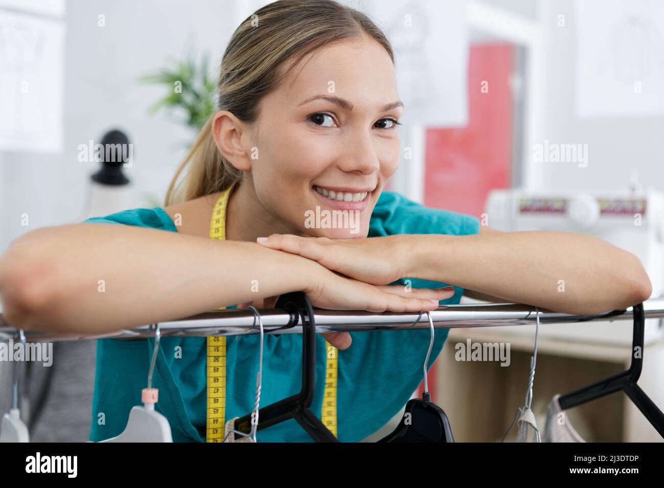 young female tailor posing against clothing rack Stock Photo - Alamy
