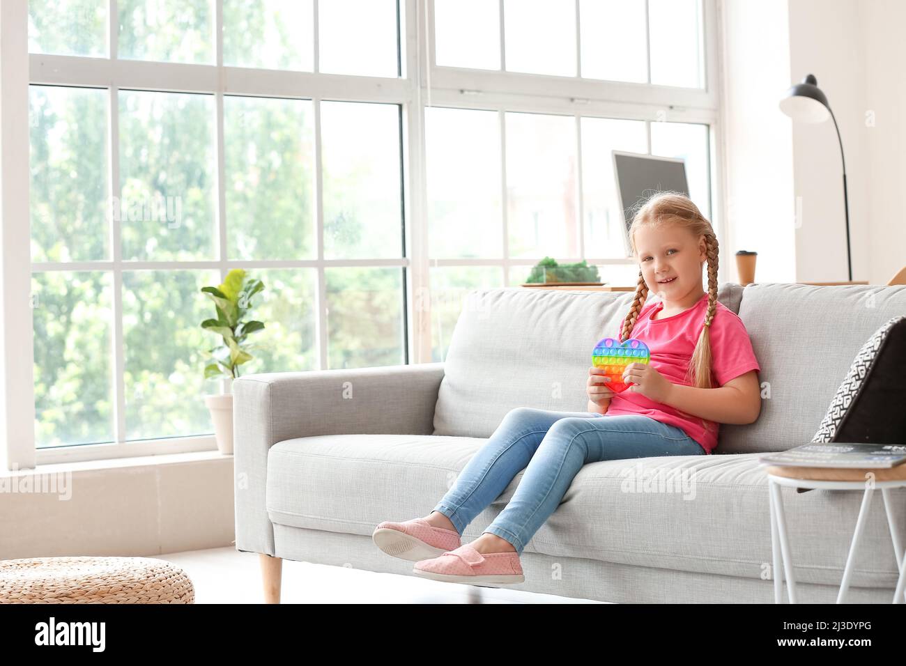 Girl sitting on sofa and holding pop it fidget toy in light room Stock ...