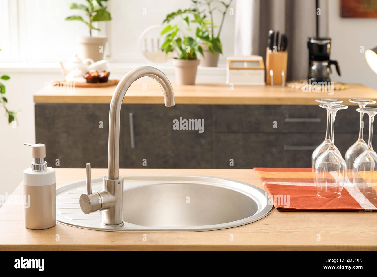 Wooden counter with silver sink, dish wash detergent and glasses in ...