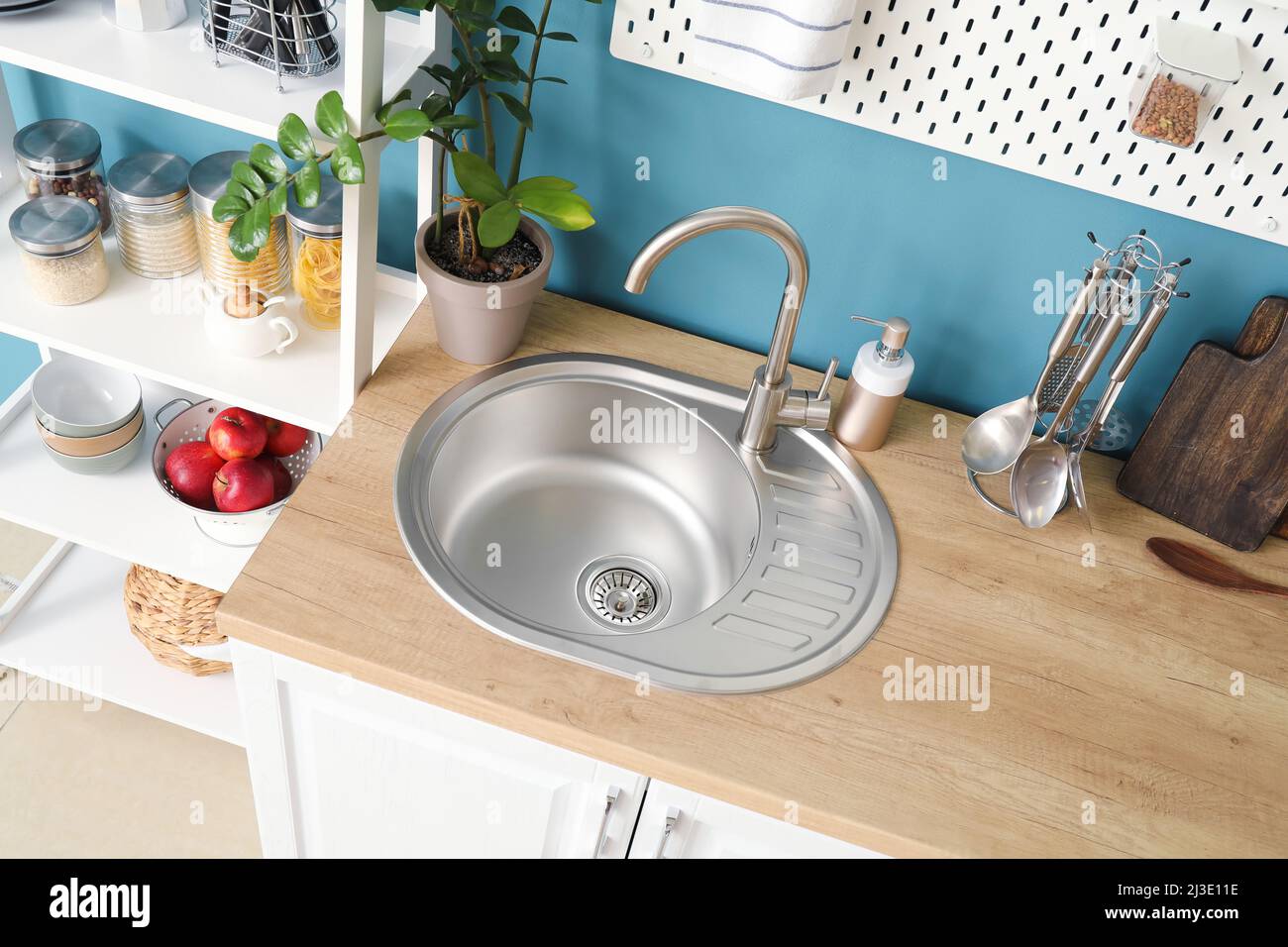Wooden counter with silver sink, cookware, shelving unit and dish soap ...